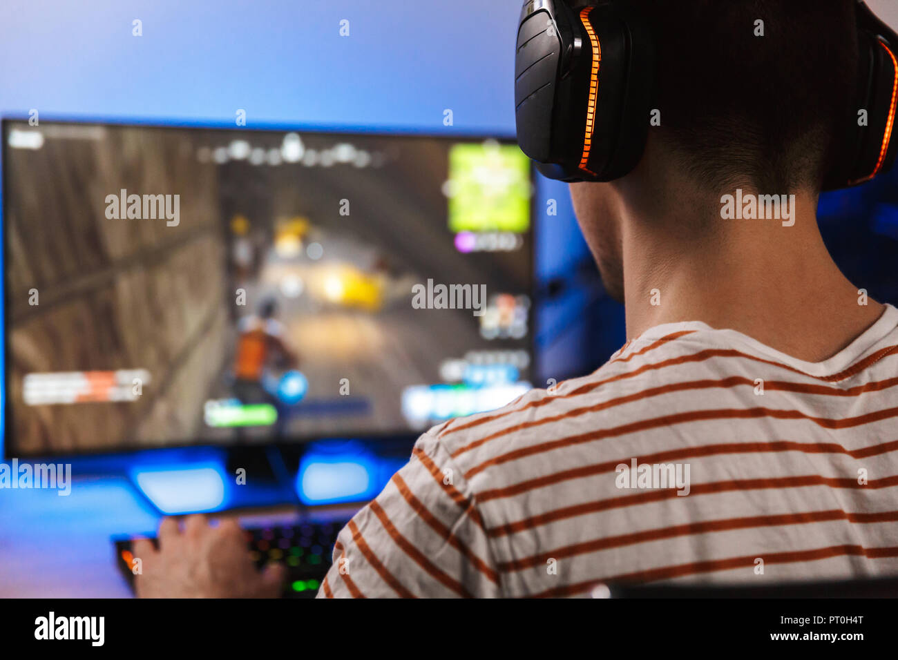 Back view of gamer playing video games on computer while sitting by the ...