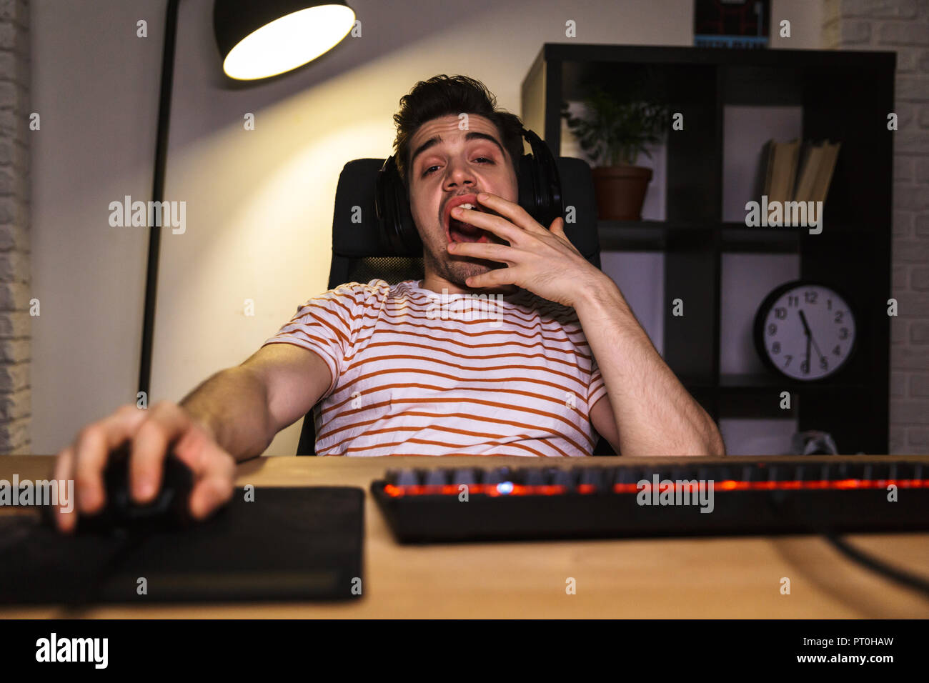 Bored gamer yawns and playing video games on computer while sitting by ...