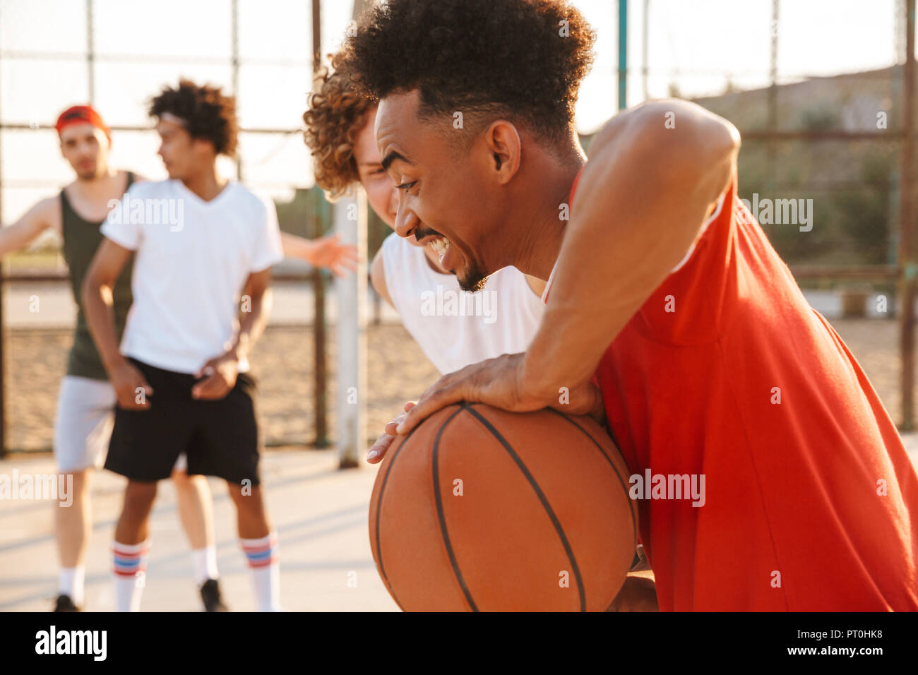 Portrait of energetic sporty men playing basketball at the playground ...