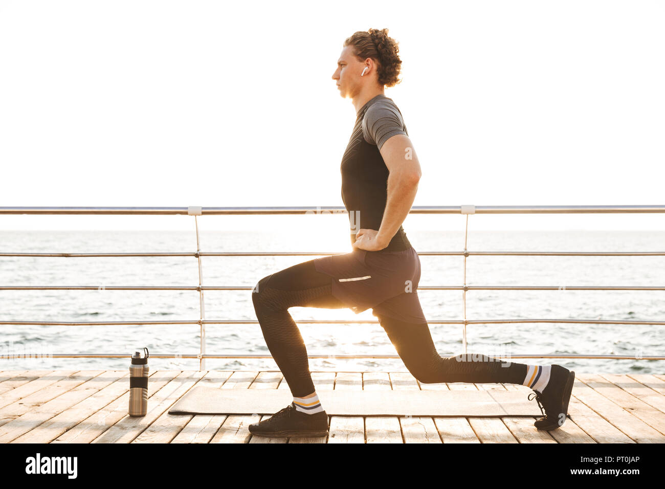 Portrait of a healthy sportsman doing lunges exercises on a fitness mat ...