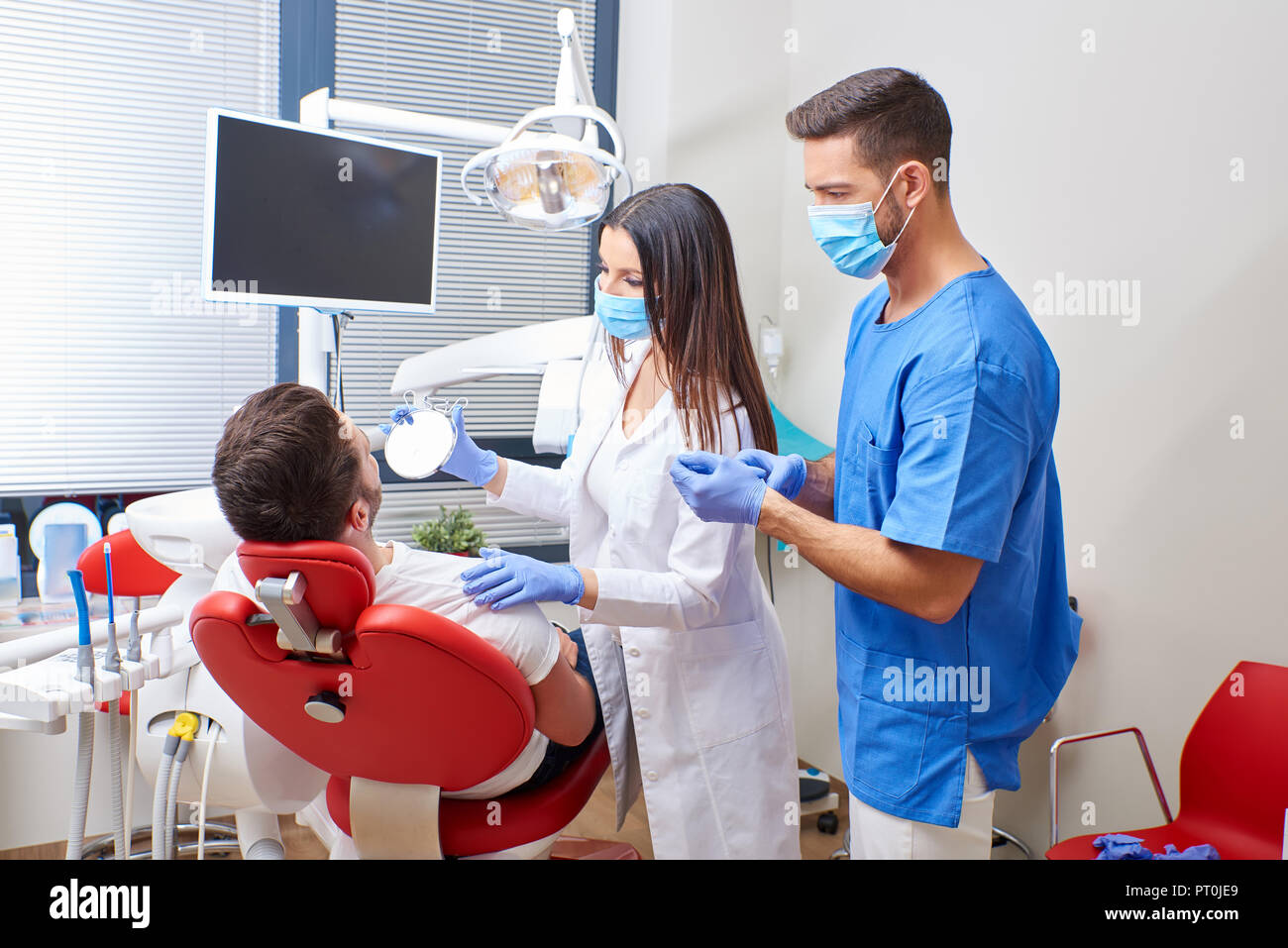 A handsome dentist with a beautiful assistant examining the patient in ...