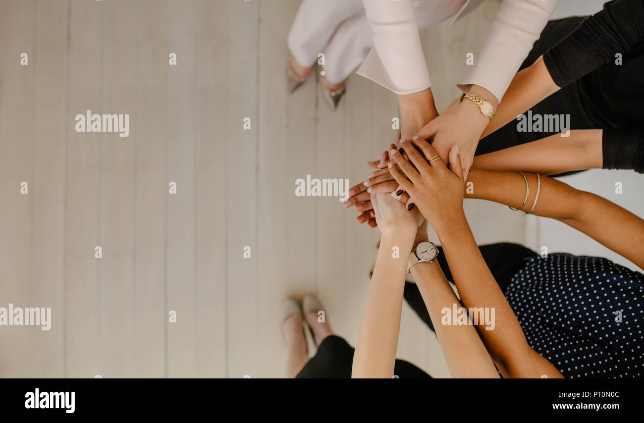 Top view image of group of young women colleagues putting their hands ...