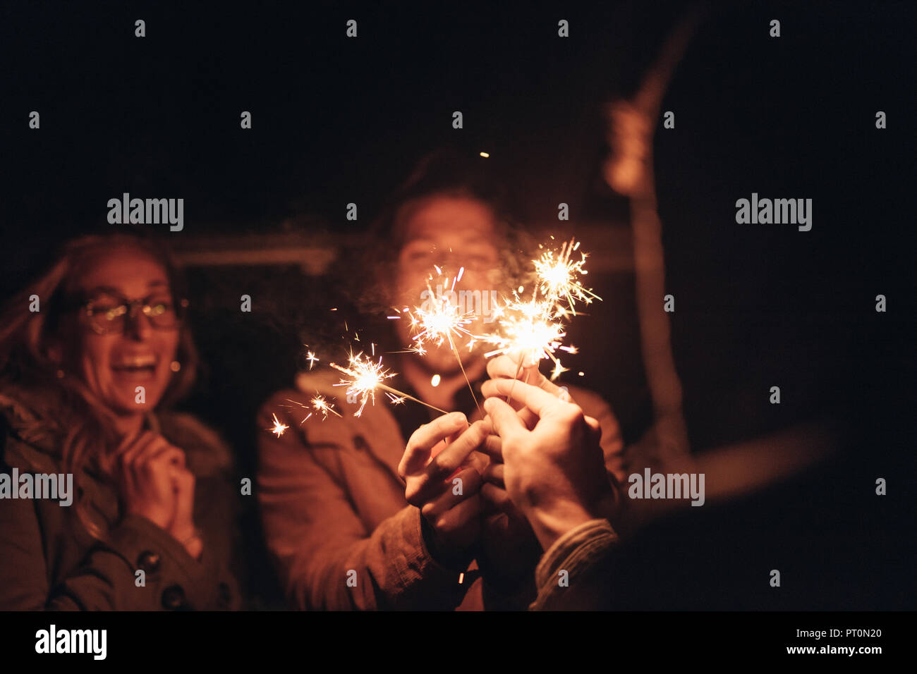 Group of friends lighting fire sparkle sticks in the dark and enjoying ...