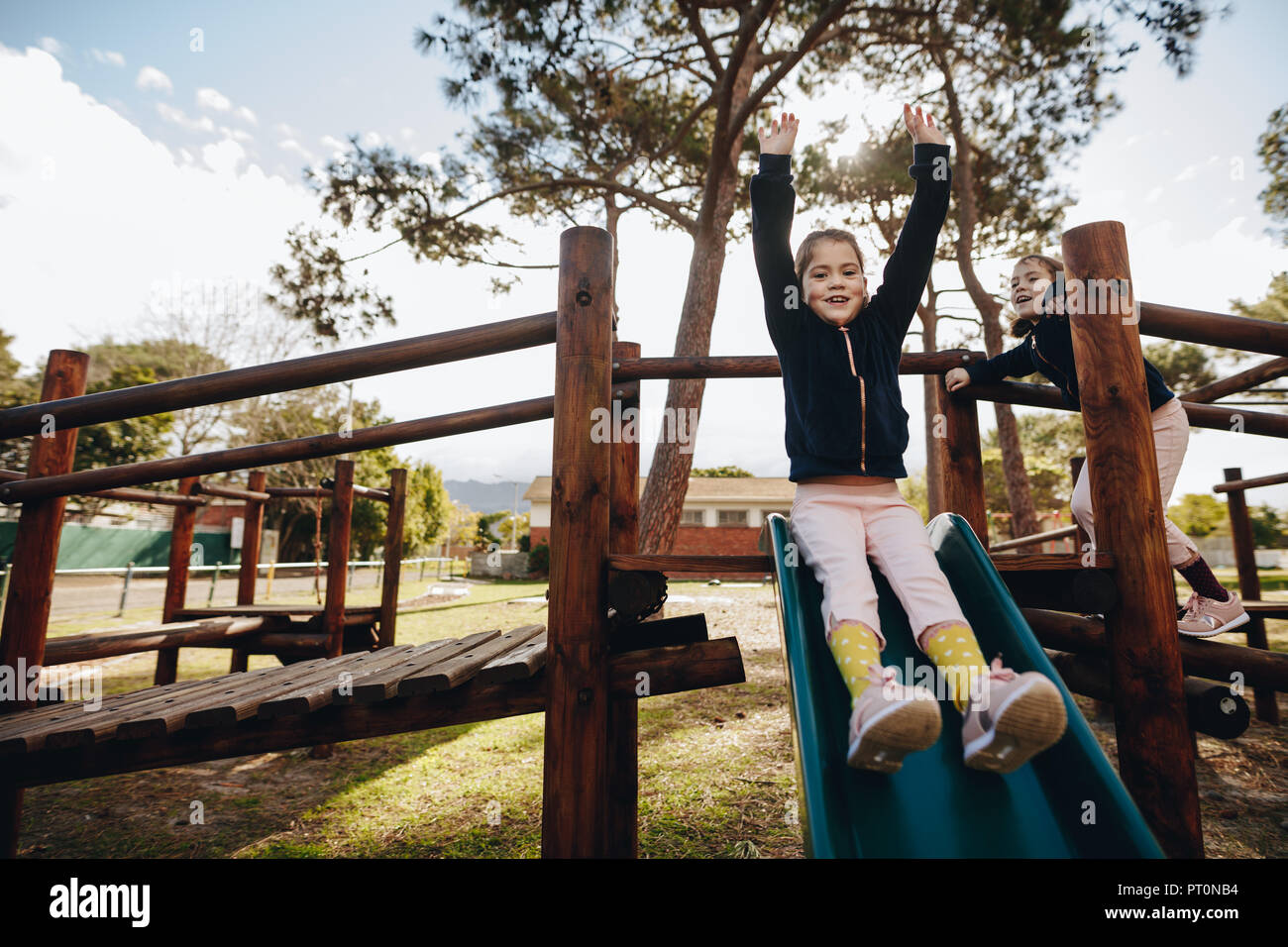 Two active girls playing together outdoors on the slide at the garden ...