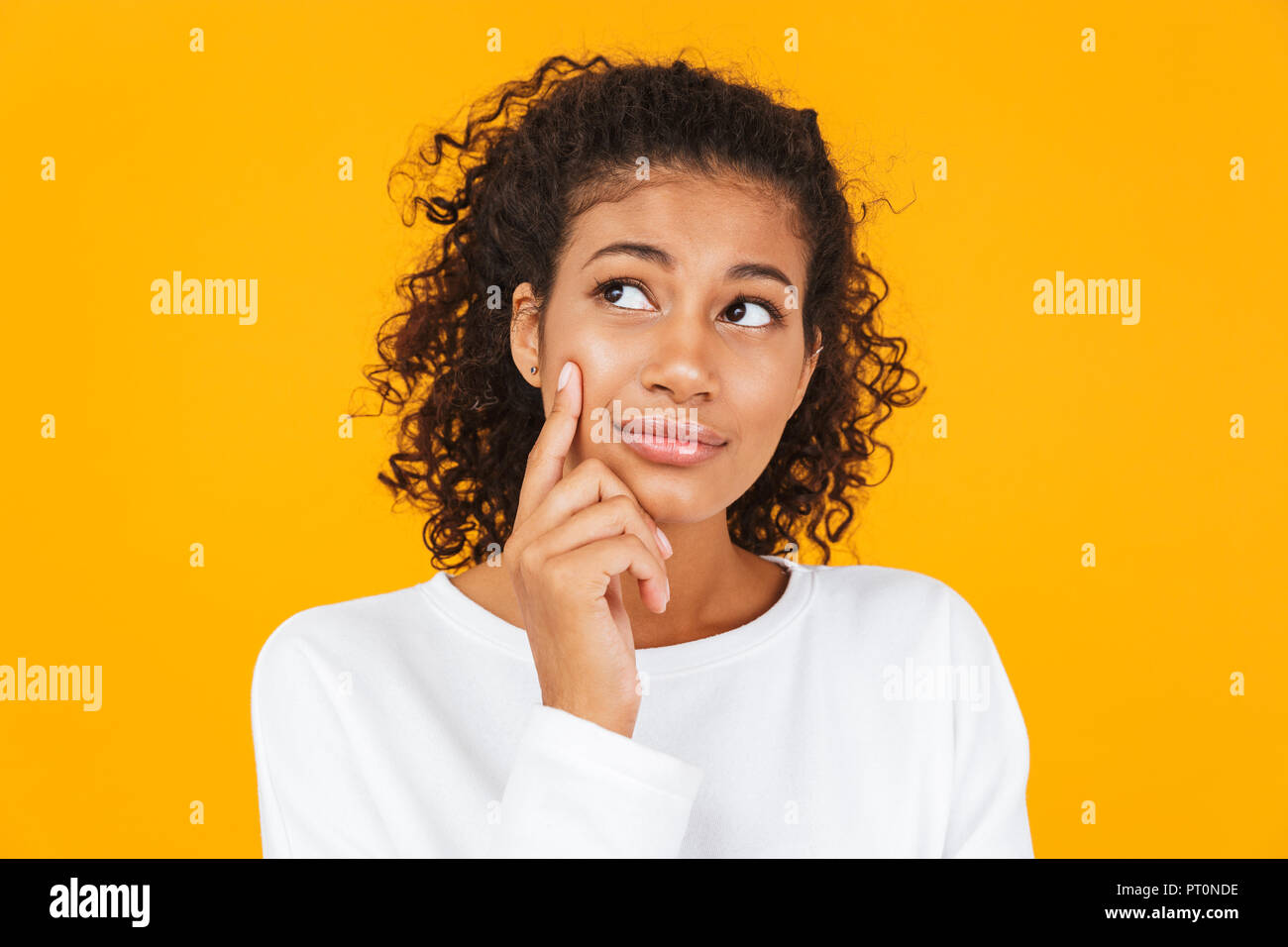 Portrait of a thoughtful young african woman standing isolated over yellow background, looking ...
