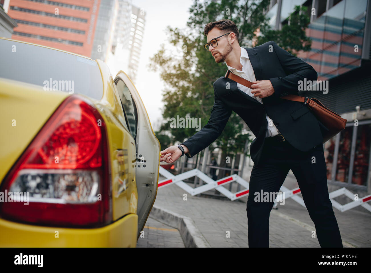 Entrepreneur opening the door of a taxi standing on the pavement. Man ...