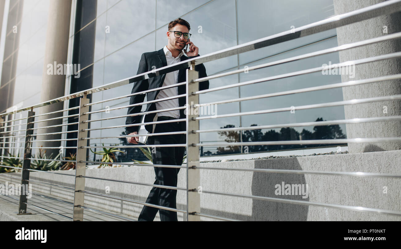 businessman walking out of office carrying a laptop and talking over ...