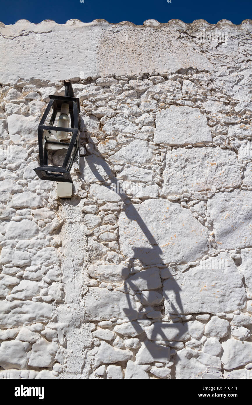 Stone wall painted white with an old broken lantern and its shadow ...