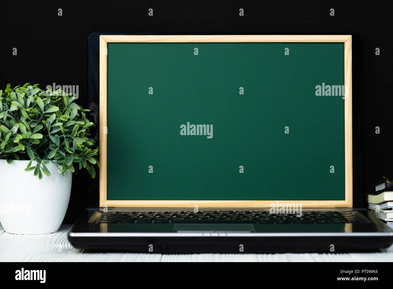 Notebook laptop computer with green chalkboard screen and pile of ...