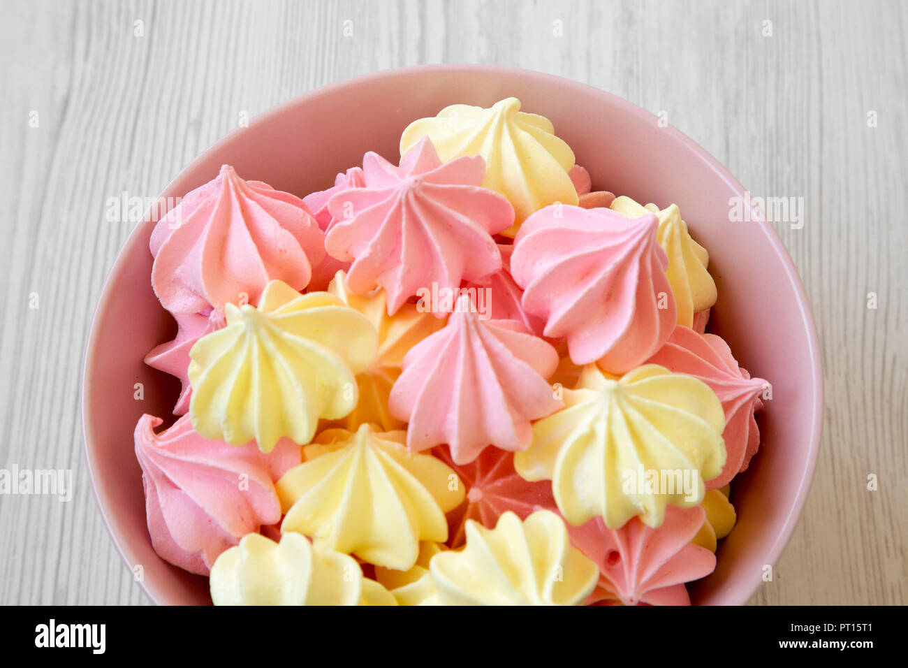 Mini meringues in a pink bowl on a white wooden background, side view ...