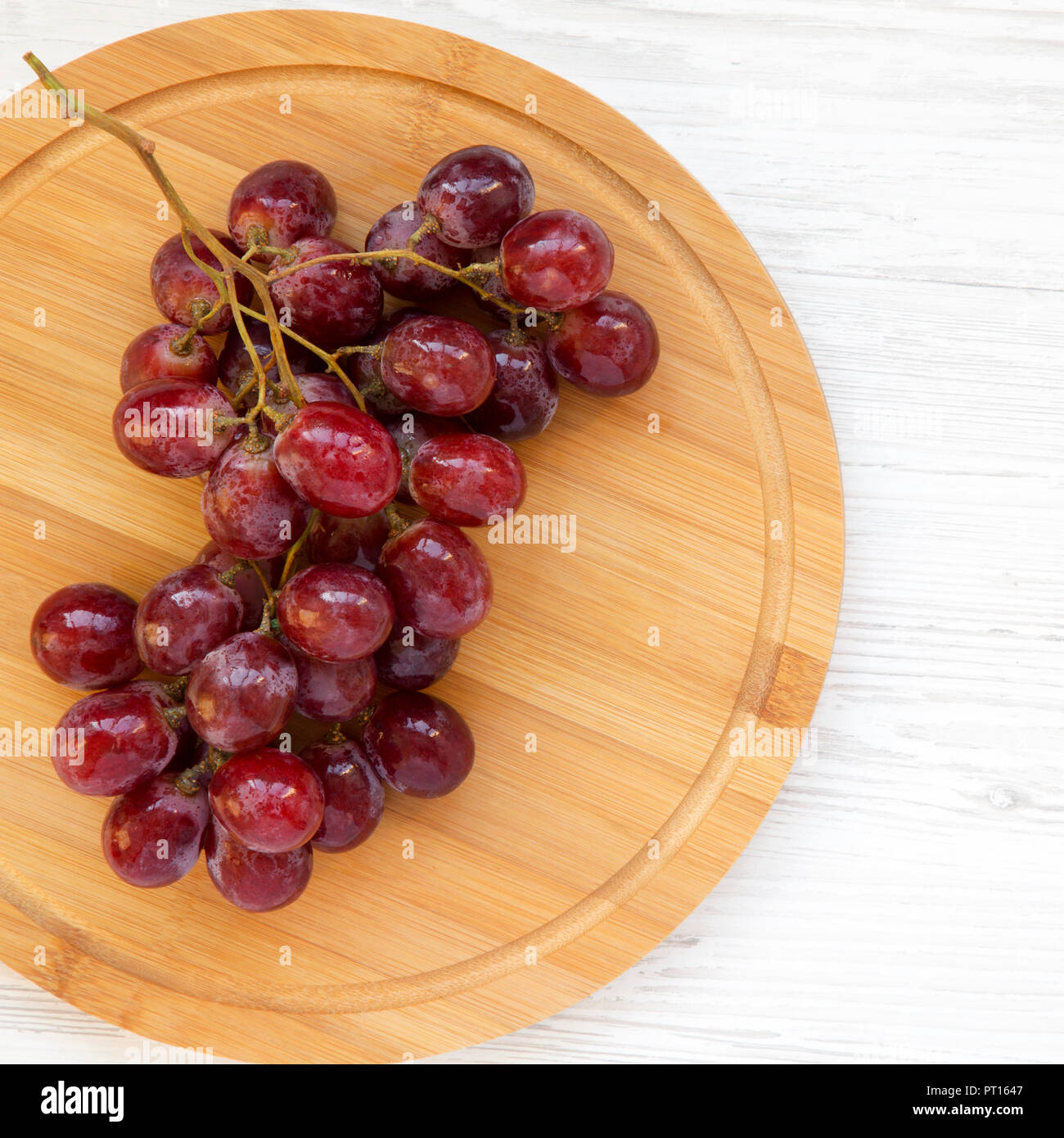Bunch of ripe red grape on a round bamboo board on white wooden ...