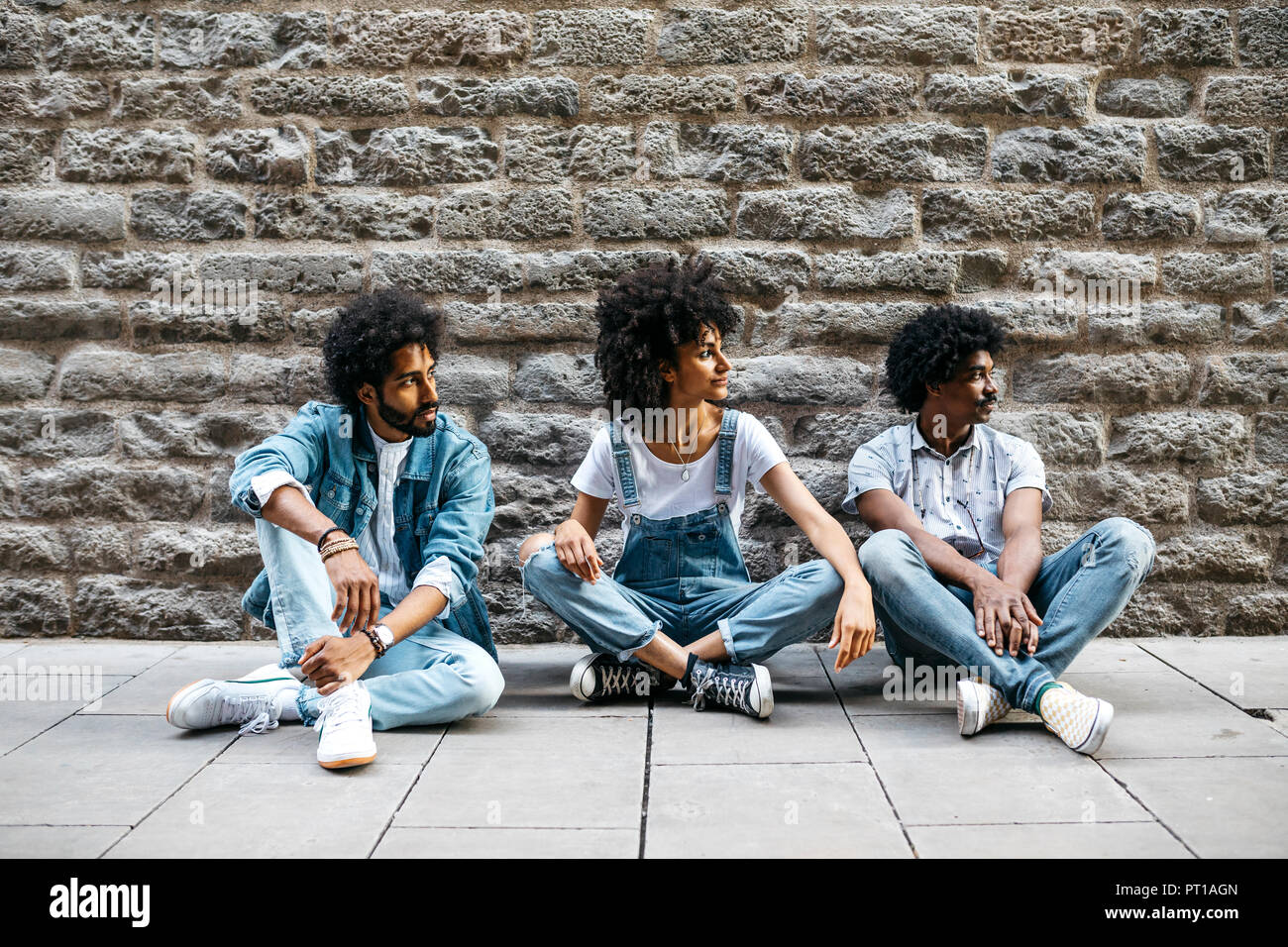 Three friends sitting together on the ground watching something Stock ...