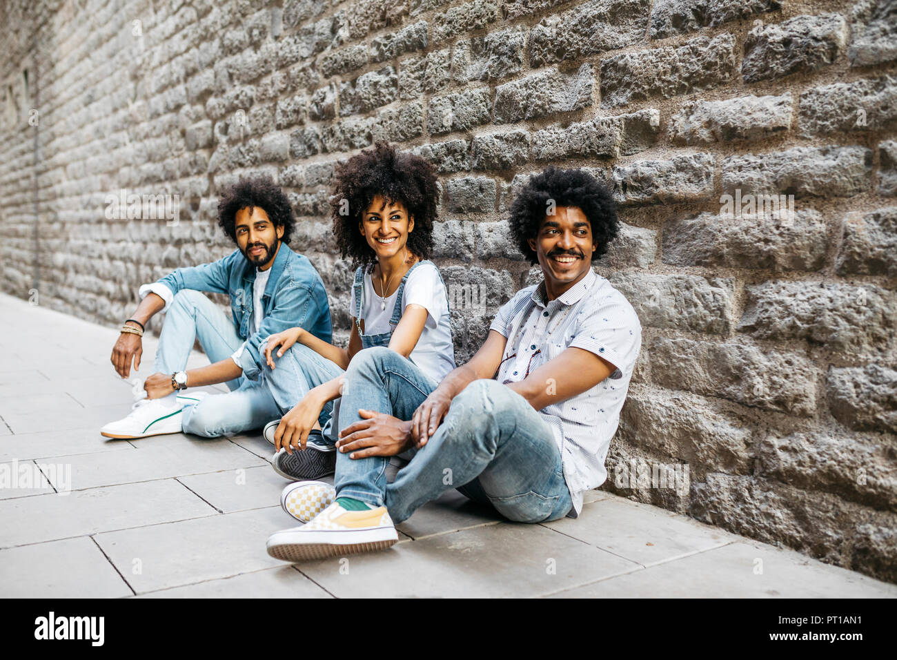 Three friends sitting together on the ground watching something Stock ...