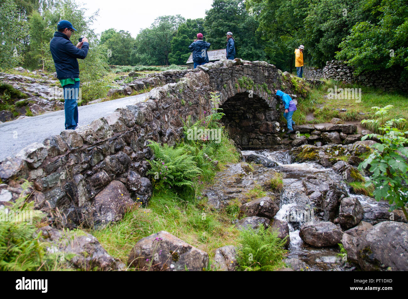 People standing on small stone arched bridge called Ashness Bridge over ...