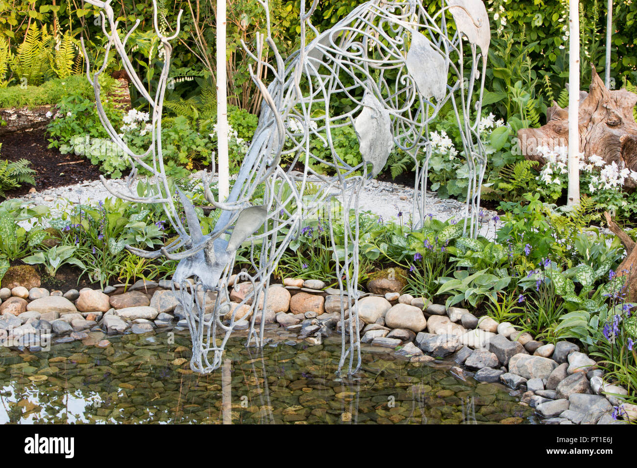 Metal stag sculpture drinking from a pond surrounded by pebbles ...
