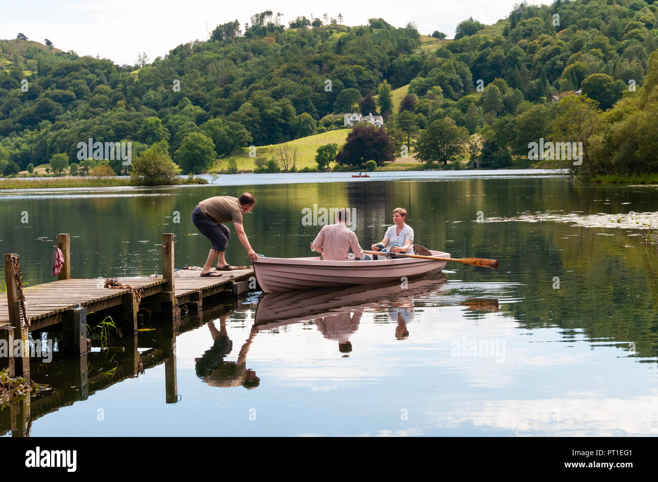 Two men in a rowing boat with a third pushing them off from a pontoon ...