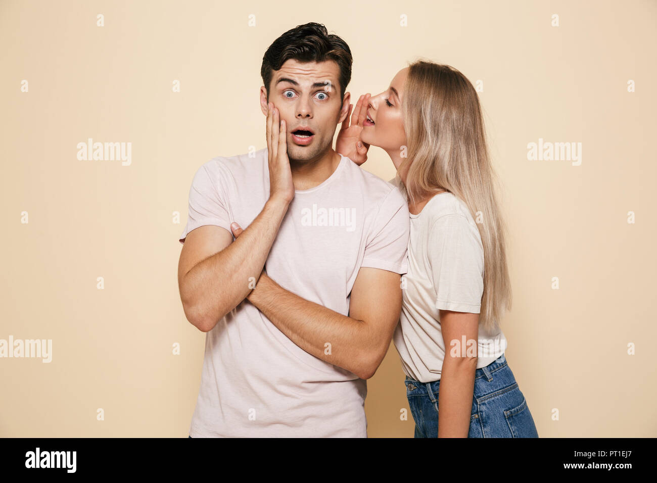 Portrait of a shocked young couple standing together over beige ...