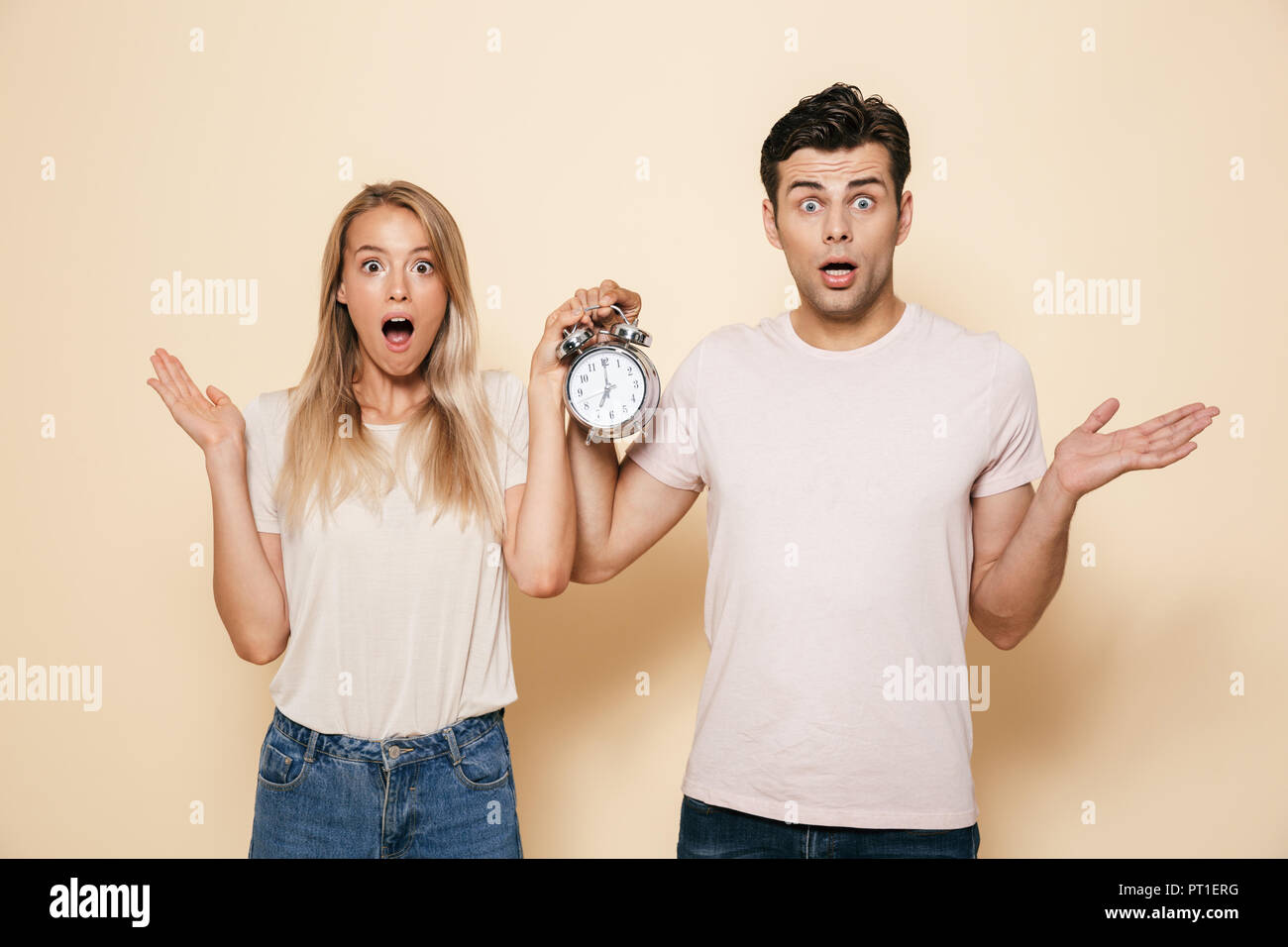Photo of shocked young loving couple holding alarm clock isolated ...