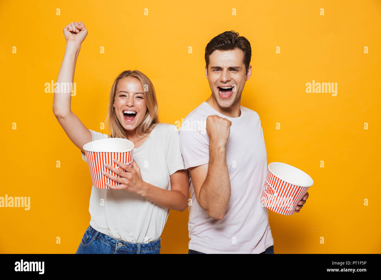 Cheerful young couple standing isolated over background, eating popcorn ...