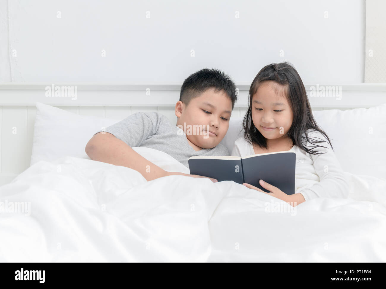 Brother and sister read book on bed together, education concept Stock ...