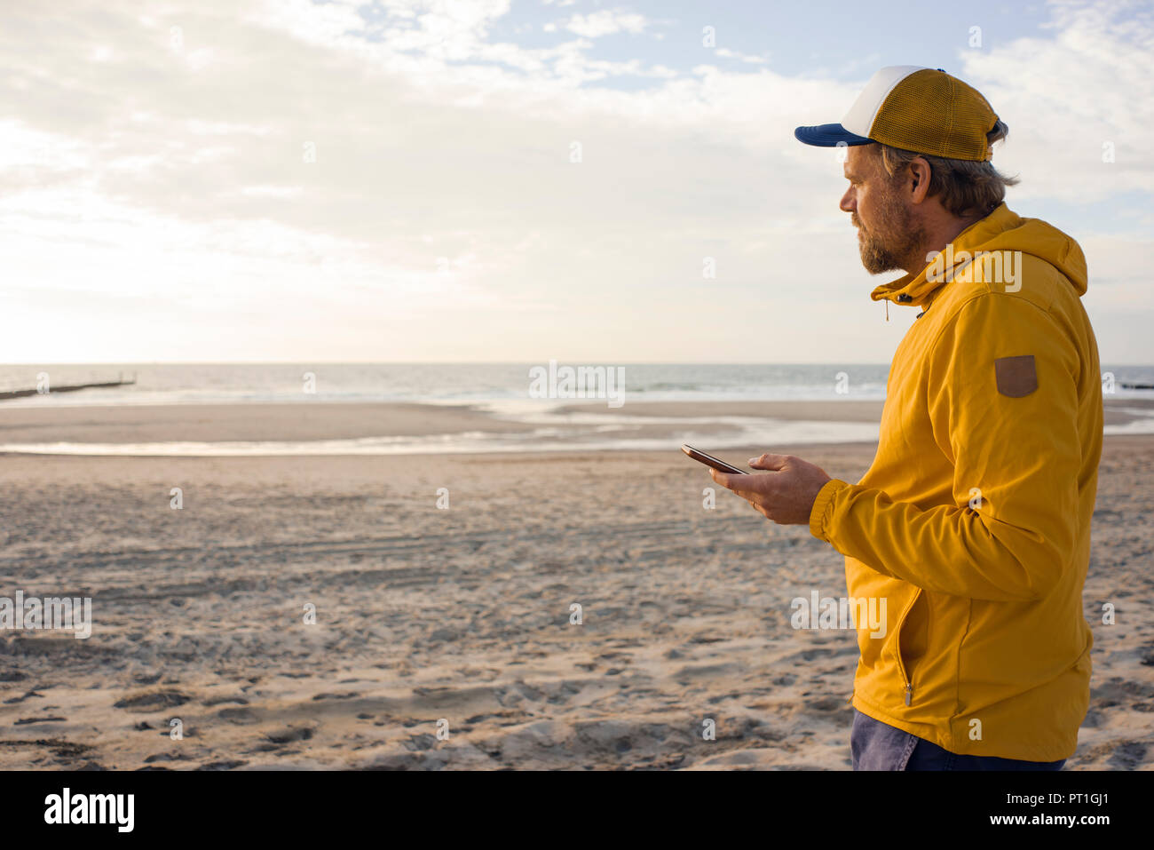 Man in yellow jacket, using smartphone on the beach Stock Photo - Alamy