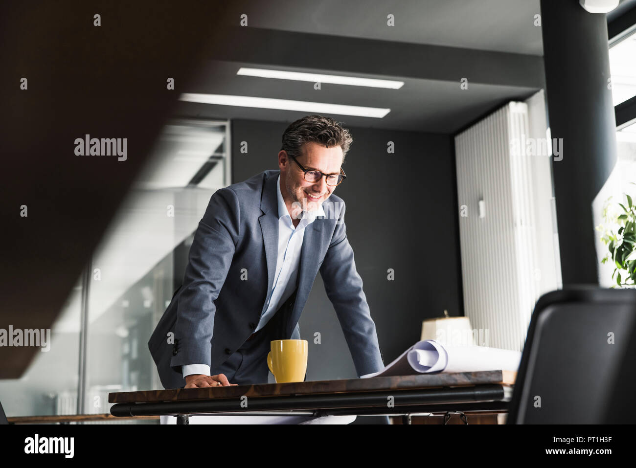 Smiling businessman in office looking at plan on desk Stock Photo - Alamy