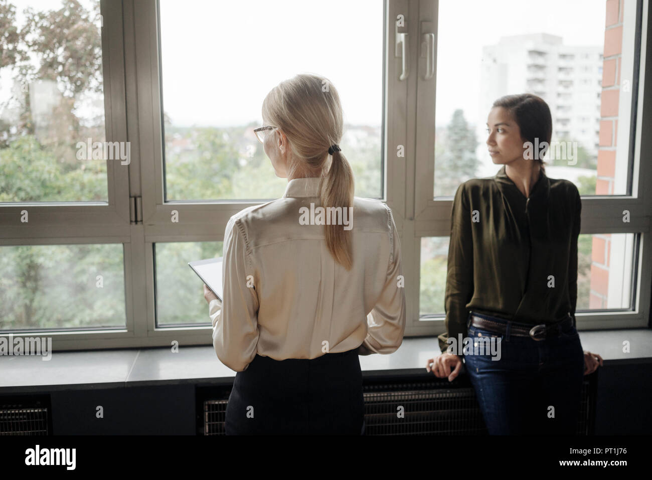Two businesswomen in office looking out of window Stock Photo - Alamy