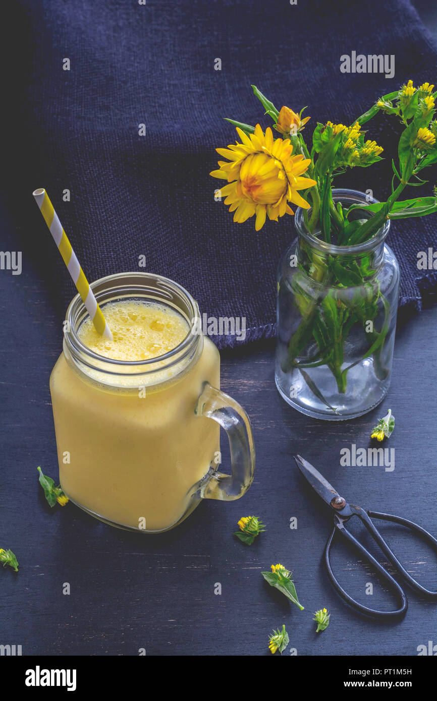 Glass of mango yoghurt smoothie and everlasting flowers in flower vase ...