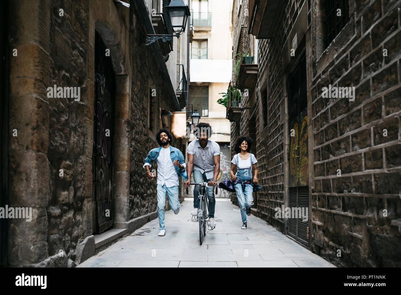 Man riding bicycle down alley friends running behind him hi-res stock ...