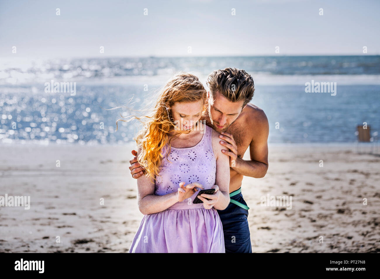 Couple on the beach looking at cell phone hi-res stock photography and ...