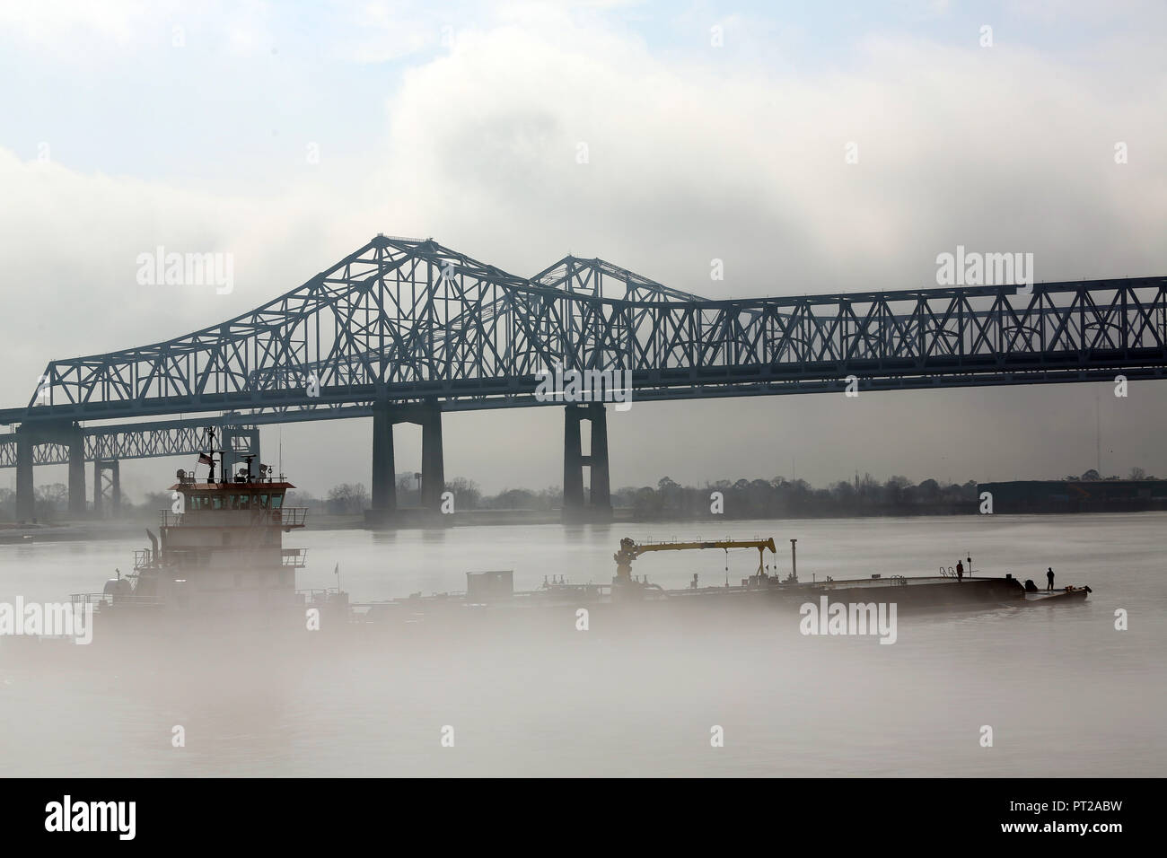 tug pushing barge under suspension bridge over foggy Mississippi River ...