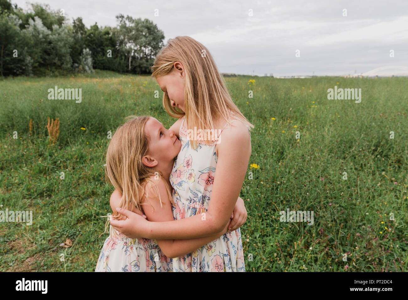 Two cute sisters are hugging each other outdoors and elder sister is ...