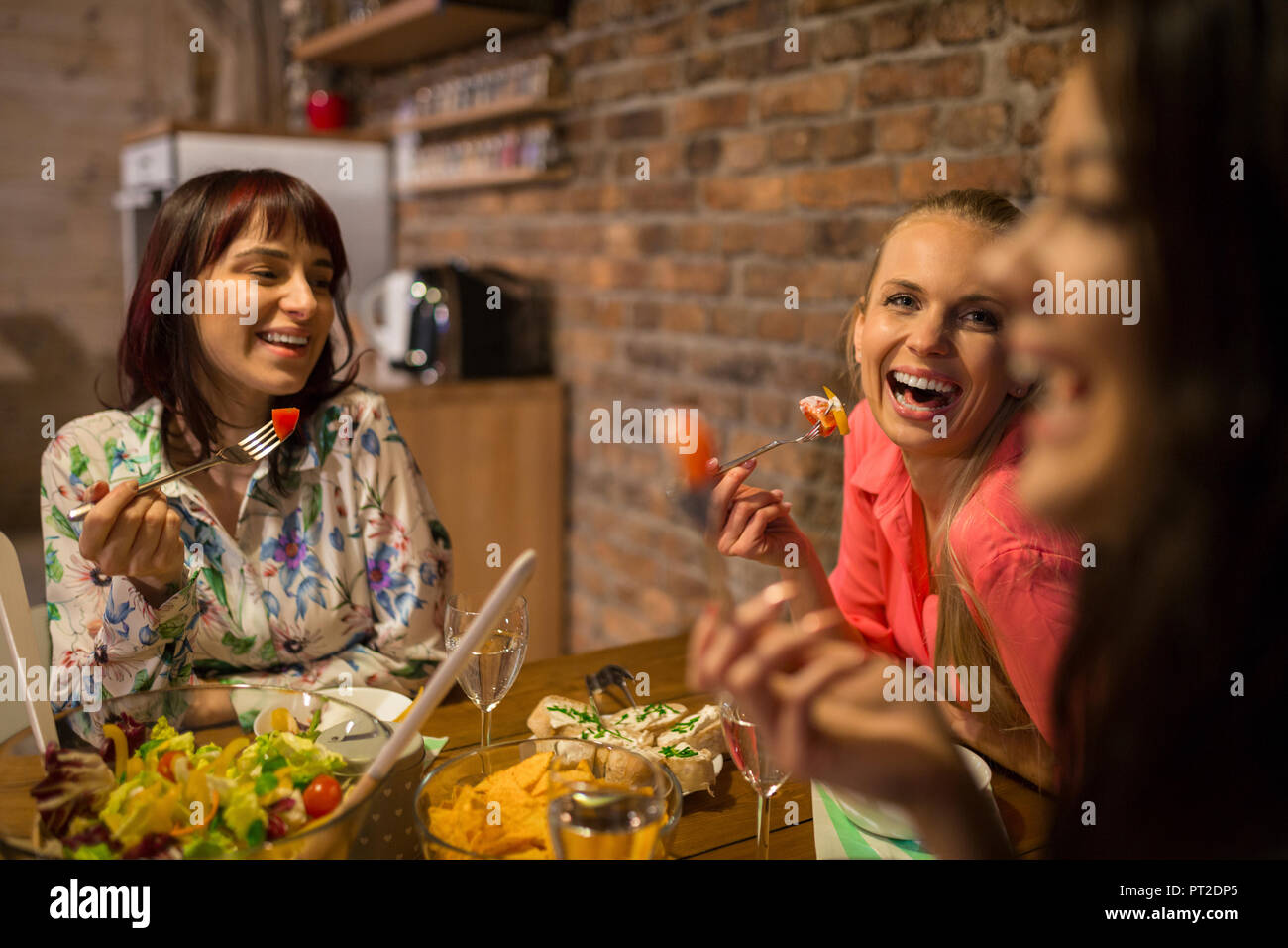 Happy female friends having dinner at home together Stock Photo - Alamy