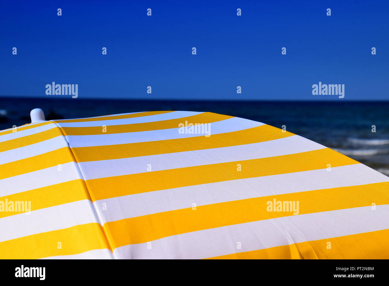 perfect beach scene, yellow and white striped parasol in front of azure ...