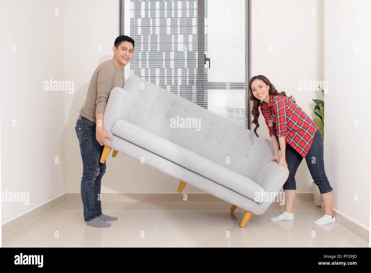 Smiling couple carrying modern chair together placing furniture moving ...