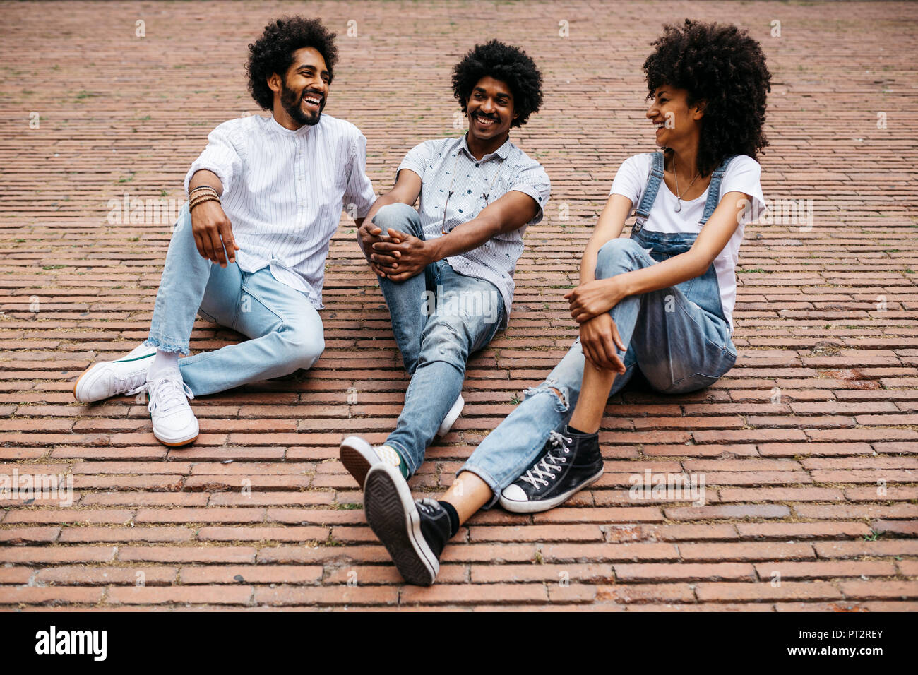 Three friends sitting on a square having fun together Stock Photo - Alamy