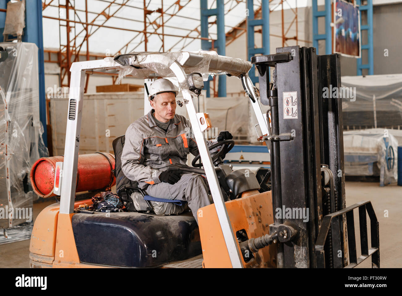 man driving a forklift through a warehouse in a factory. driver in ...