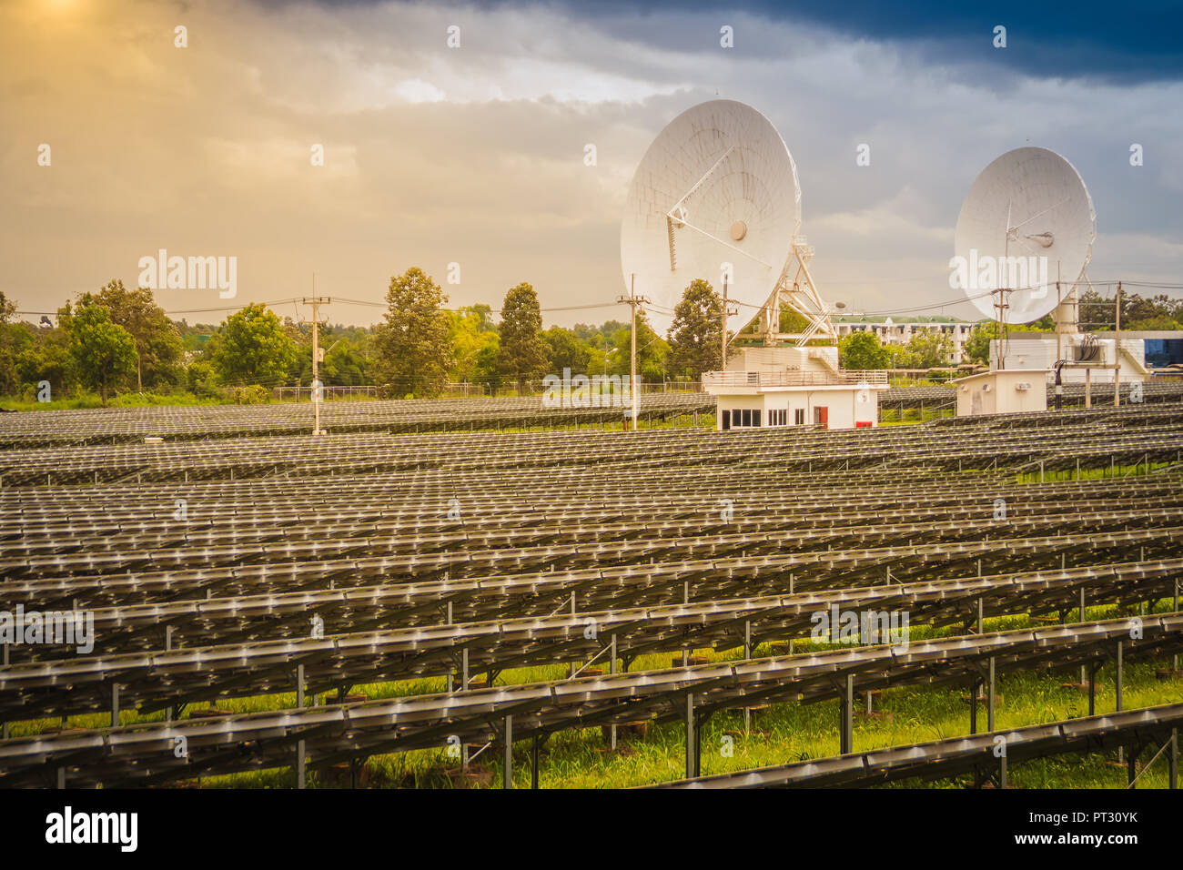 Large scale solar farm with the satellite dishes under dramatic blue ...