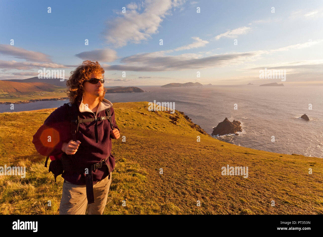 man standing on cliffs with islands in background lit from behind ...