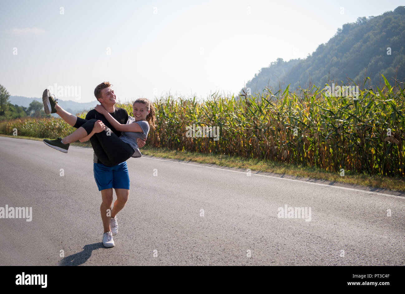 man carries a woman in his arms while jogging along a country road ...