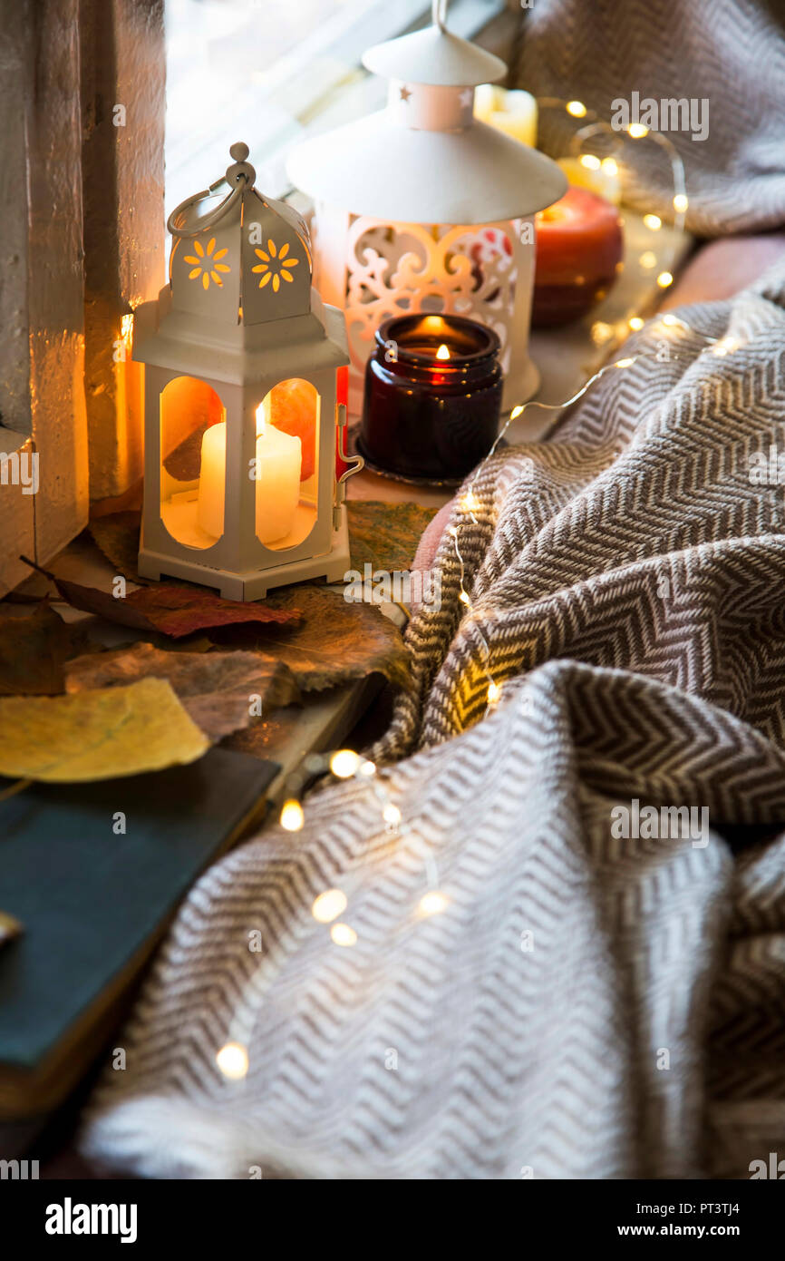 Fall still life candles and lanterns at window with lights and blanket ...