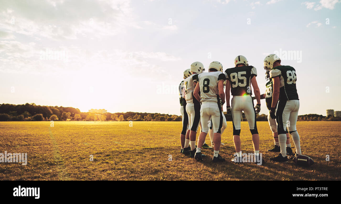 Group of young American football players standing in a circle talking ...