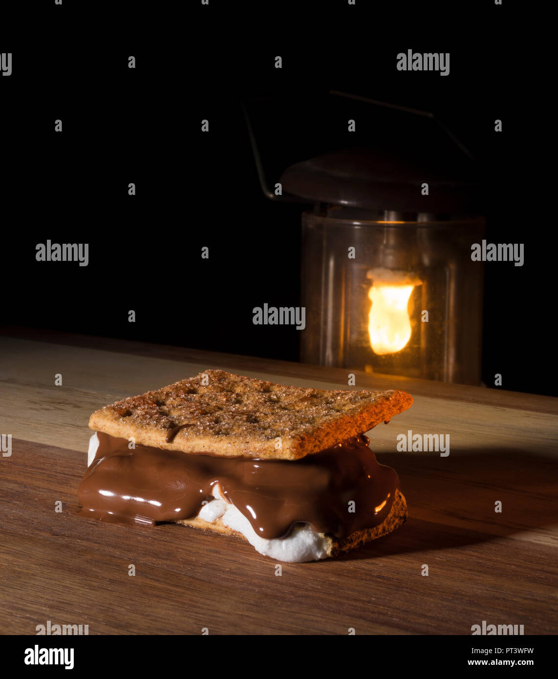 Thick smore on a wood table with a camping lantern burning behind Stock ...