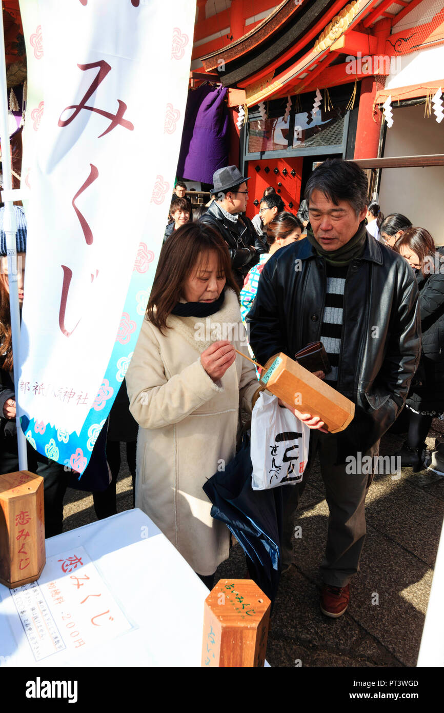 Couple shaking omikuji boxes before taking out the paper fortune slip ...