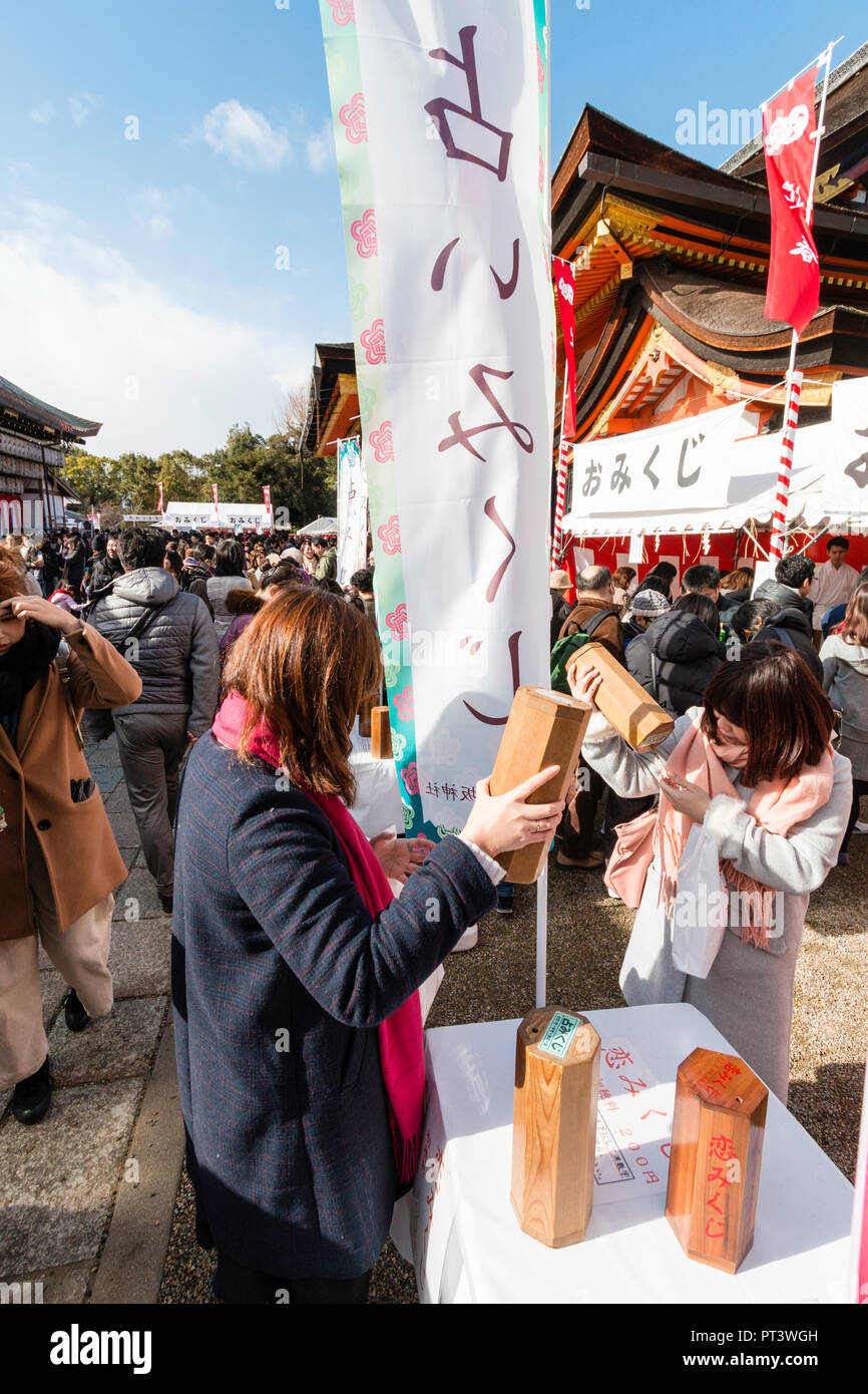 Two women shaking omikuji boxes before taking out the paper fortune ...