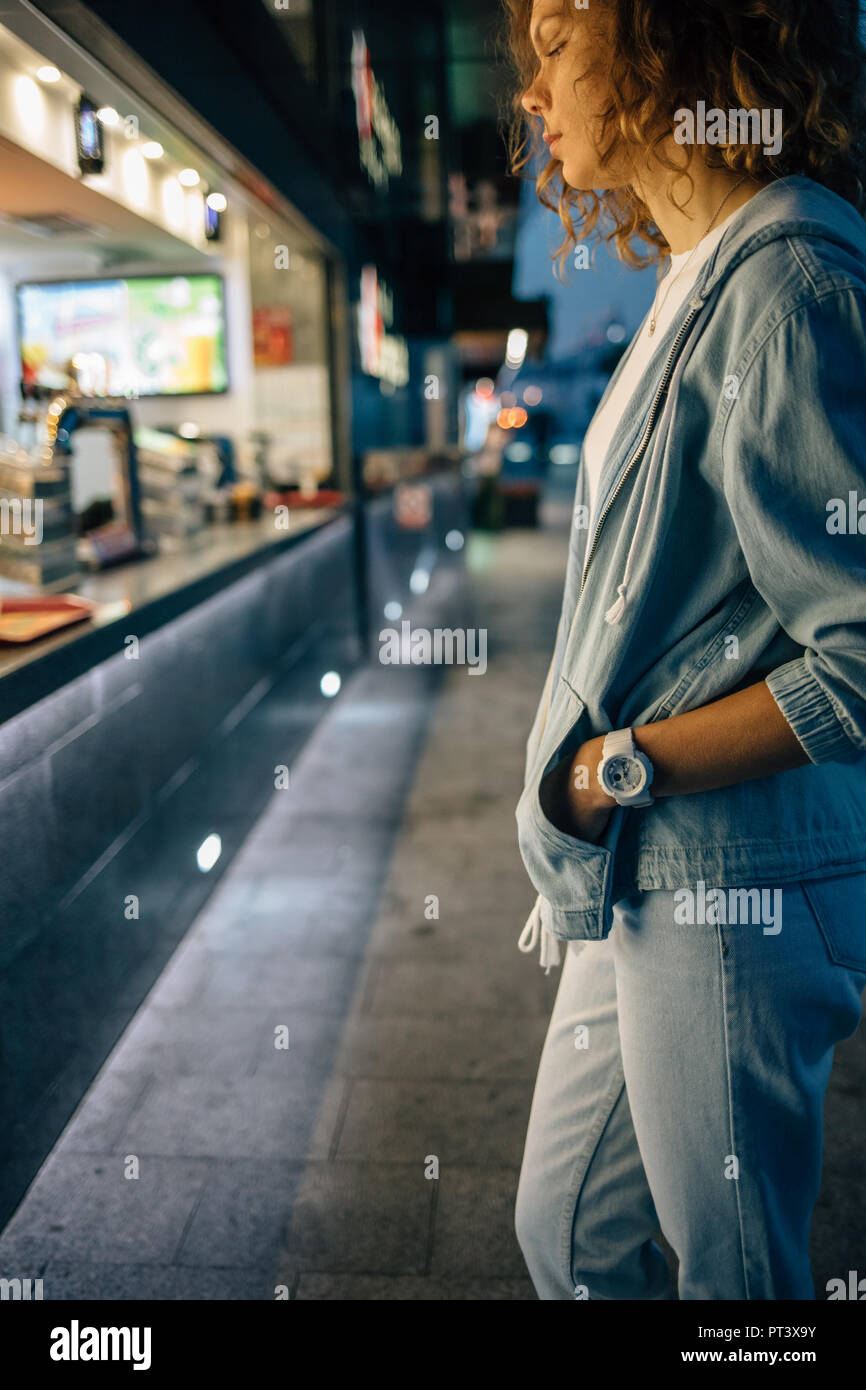 Girl choosing meal in street cafe, looking at glowing shop window ...