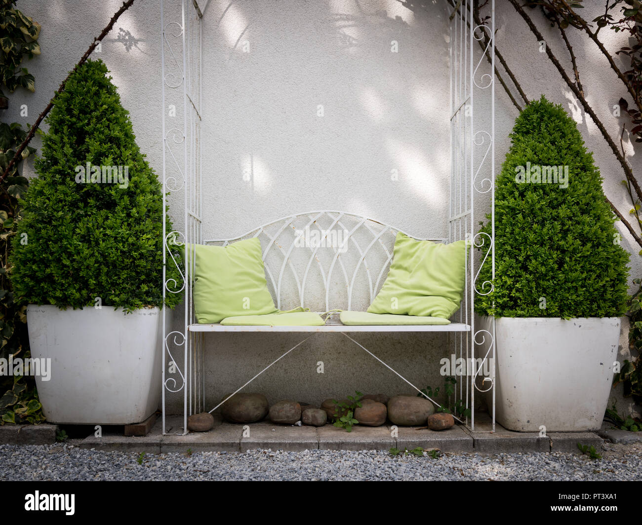 White garden bench made of iron with two green bushes in a flower pot ...