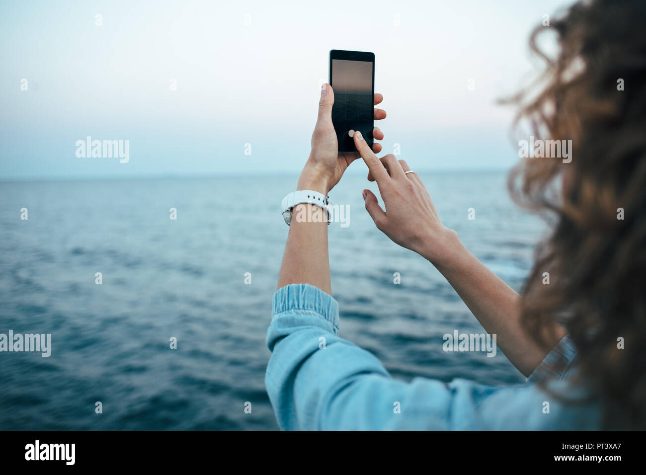 Young woman touching screen taking photo of blue sea on mobile phone ...