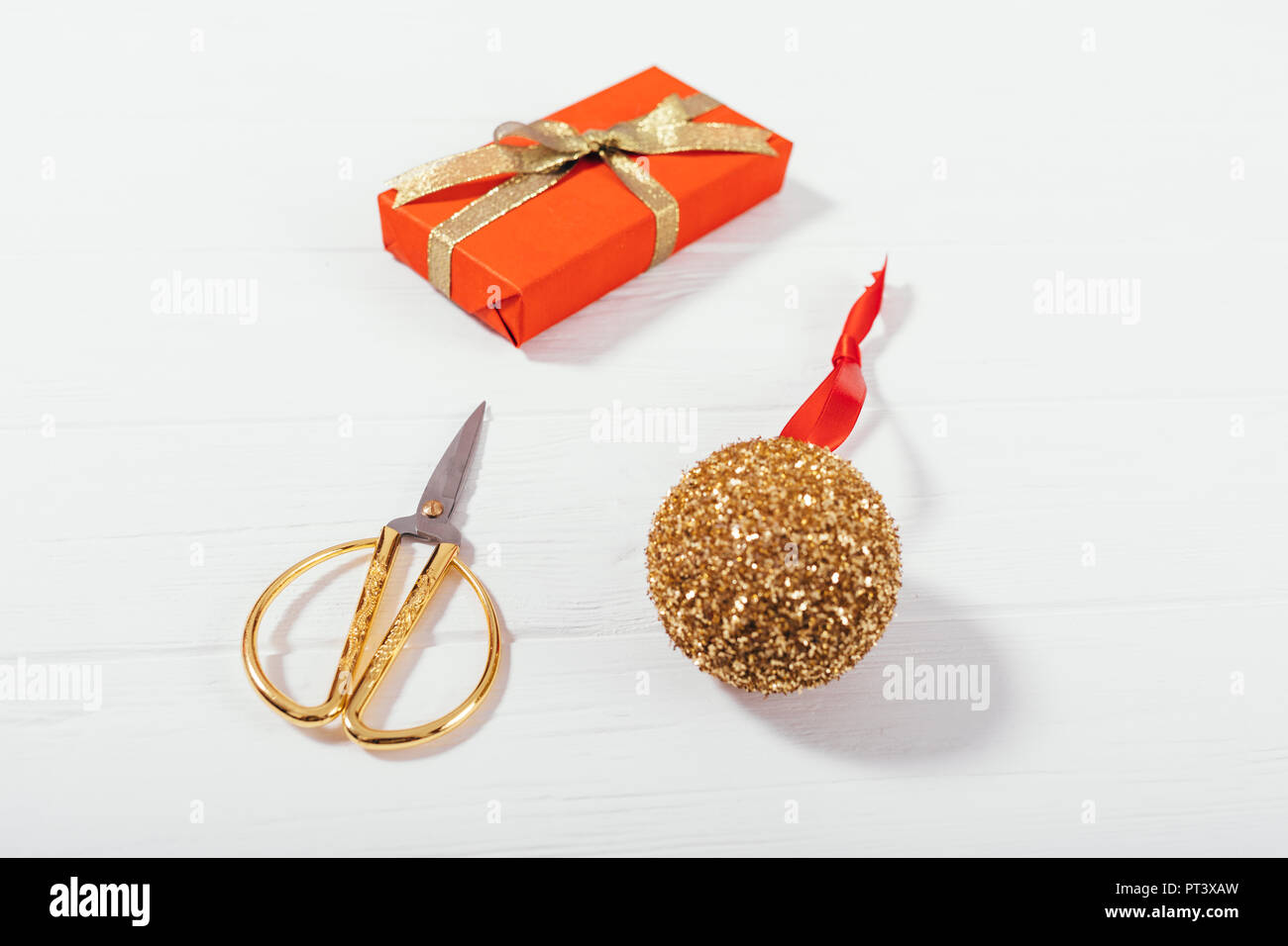 Close-up gold Christmas ball, scissors and red gift box on white wooden ...