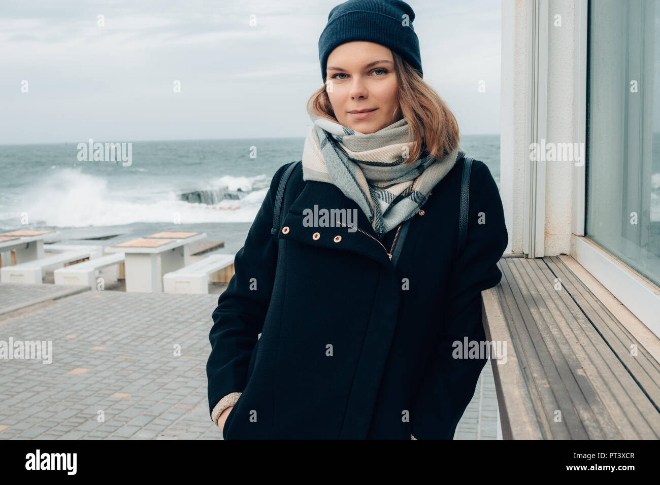 Happy stylish young woman wearing coat, beanie hat and scarf standing ...